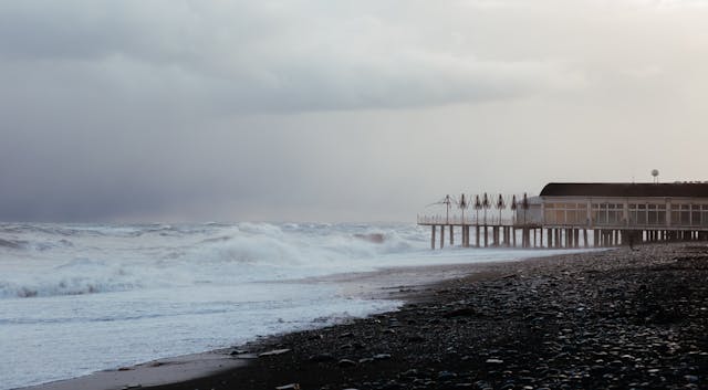 stormy sea by beach with pier